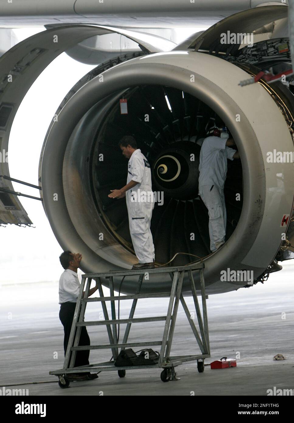 Technicians inspect the engine of a Garuda Indonesia Airbus A-330 jet ...