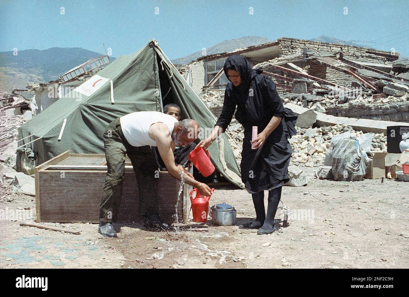 An Iranian man gets help from his wife as he cleans up outside their ...