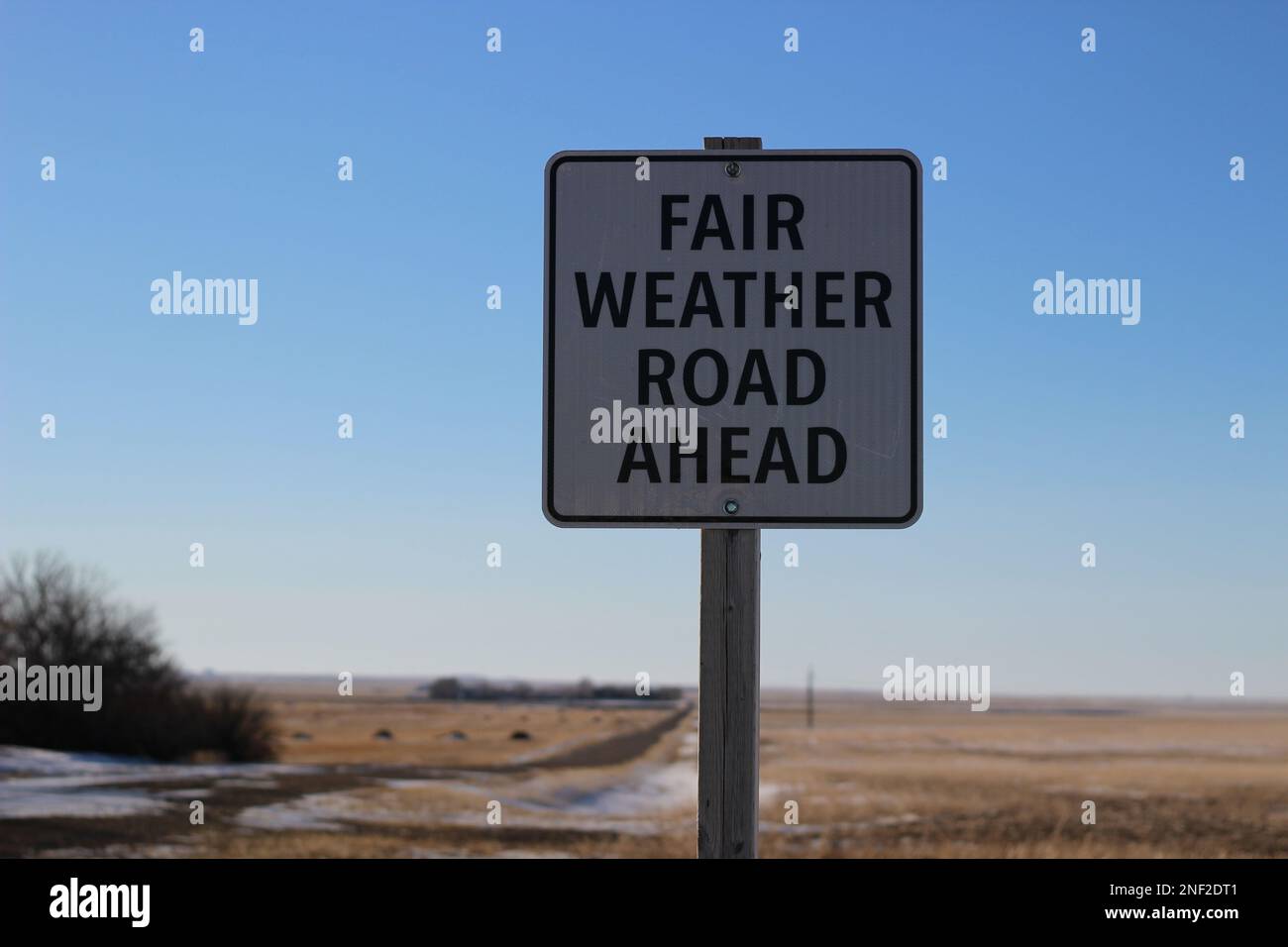 A fair weather road ahead sign along a dirt road in Canada with ...