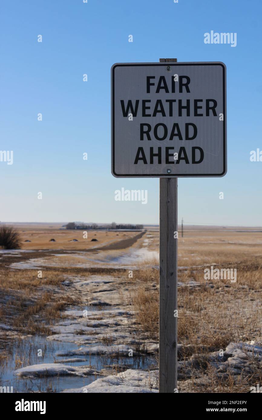 A fair weather road ahead sign along a dirt road in Canada with ...