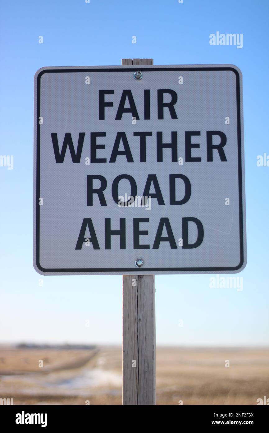 A fair weather road ahead sign along a dirt road in Canada with ...