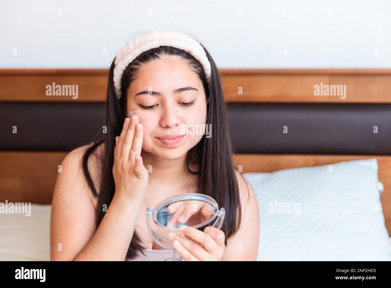 Young woman on her bed, applying anti age and anti wrinkles facial ...