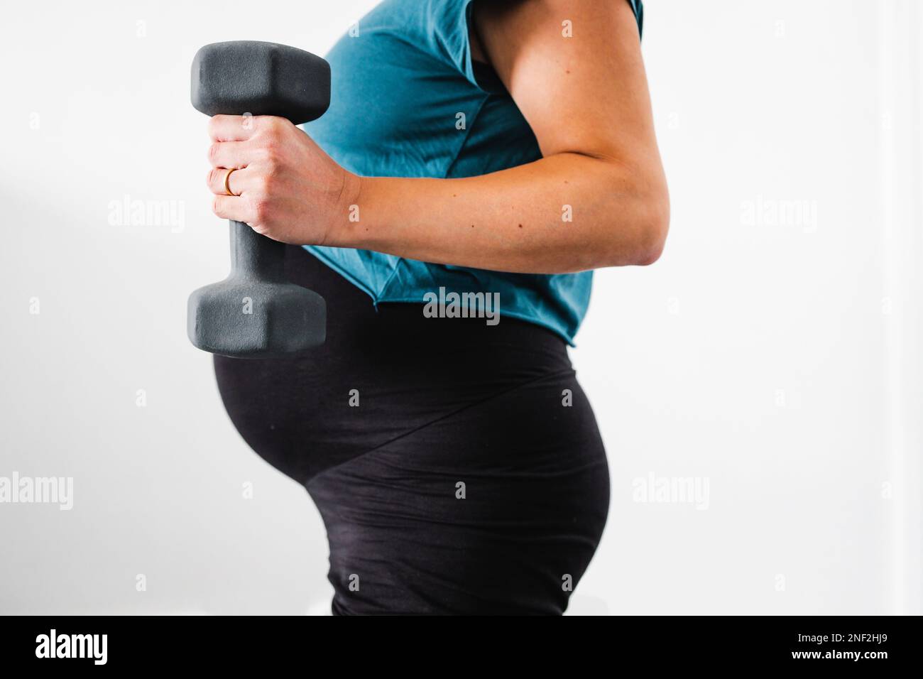 pregnant woman exercising with dumbbell in her hand and showing her ...