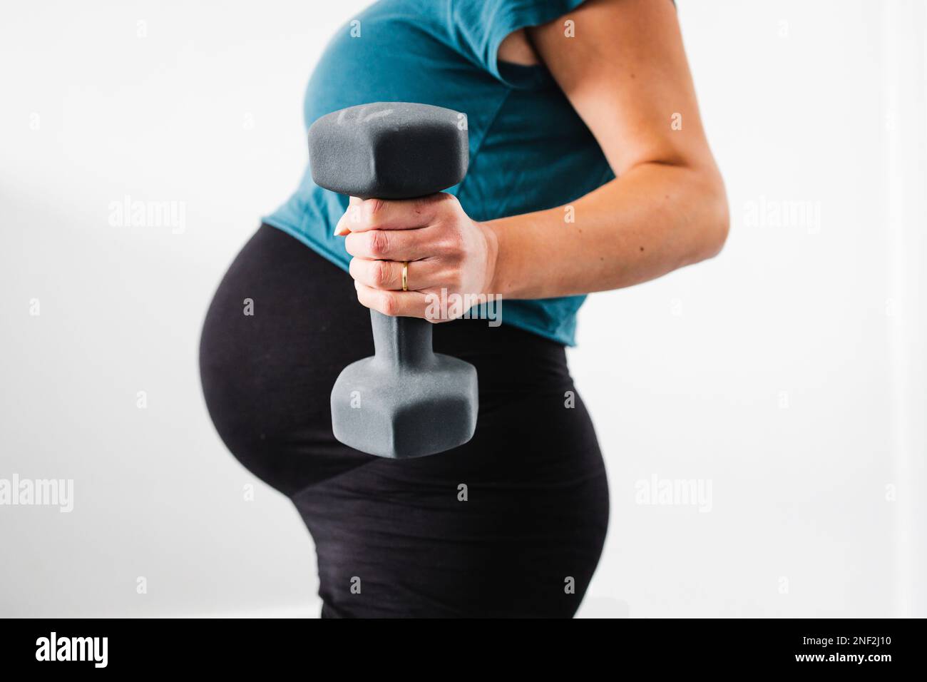 pregnant woman exercising with dumbbell in her hand and showing her ...