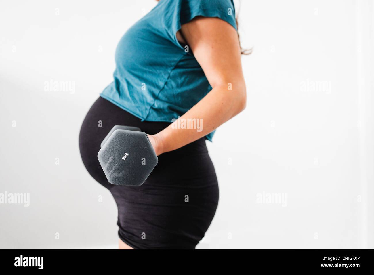 pregnant woman exercising with dumbbell in her hand and showing her ...