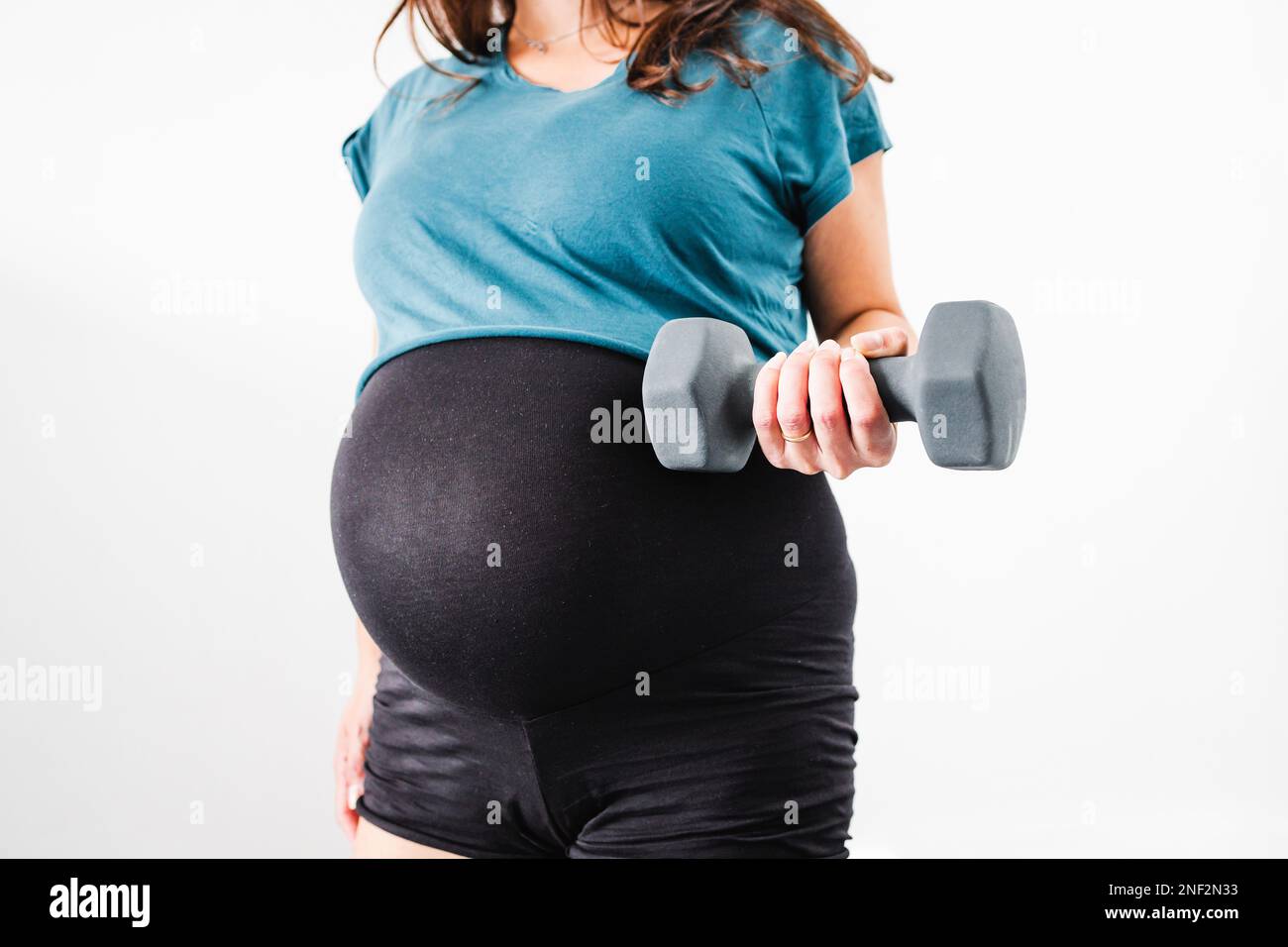 pregnant woman exercising with dumbbell in her hand and showing her ...