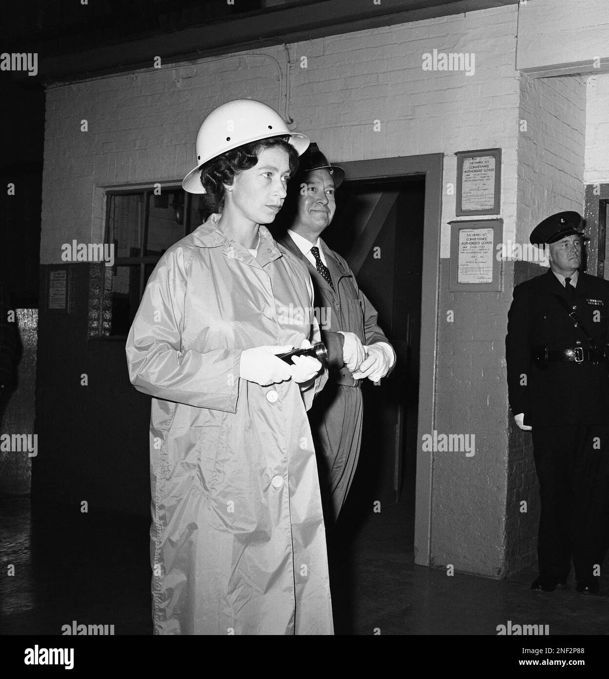 Queen Elizabeth II, dressed in a plastic raincoat, white helmet and ...