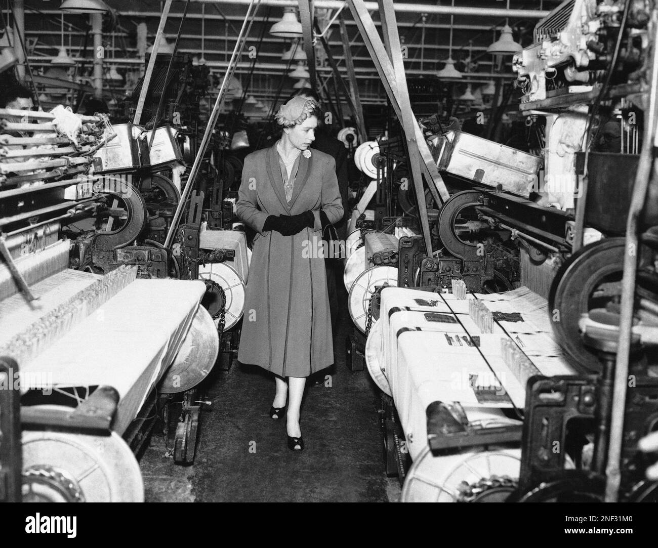 Queen Elizabeth II walks between weaving machines at the Malvern Mill ...