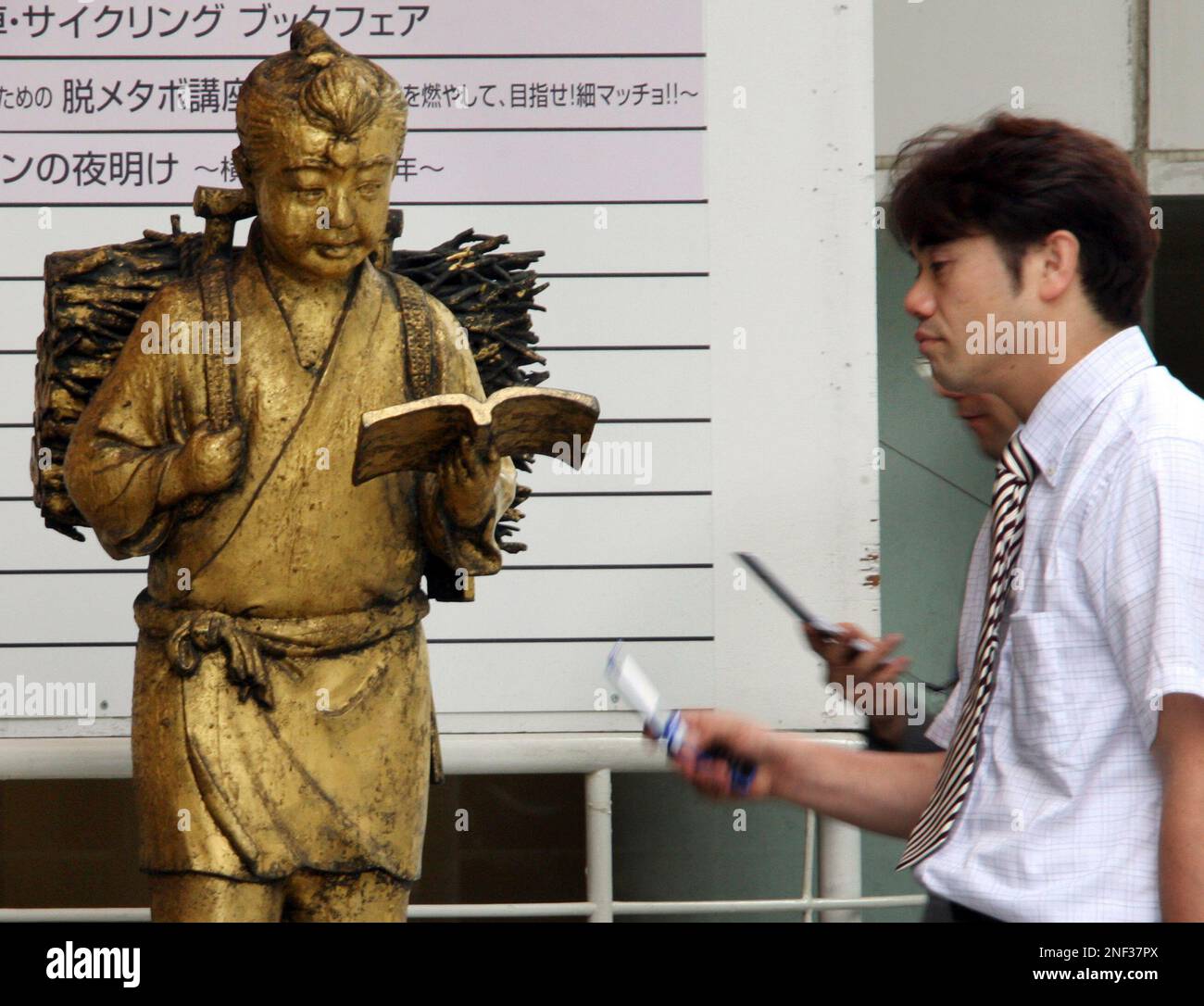 Japanese men walk by a statue of Ninomiya Kinjiro reading a book while ...