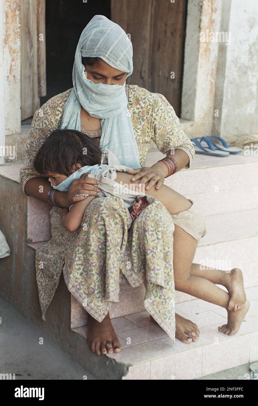 Masked to avoid infection from pneumonic plague, a mother massages her ...