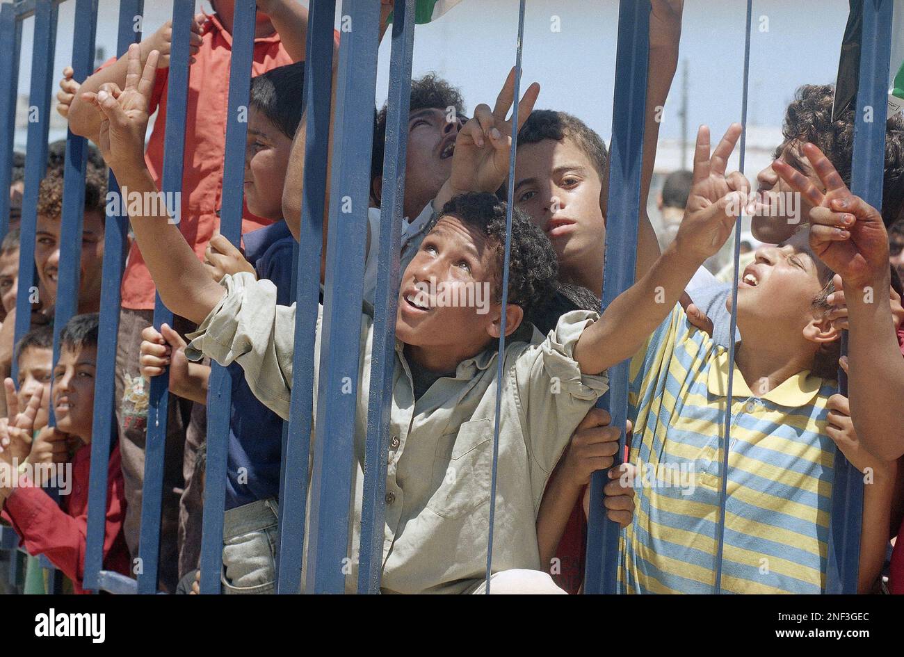 Palestinian boys make V-signs from behind a perimeter fence as they try ...