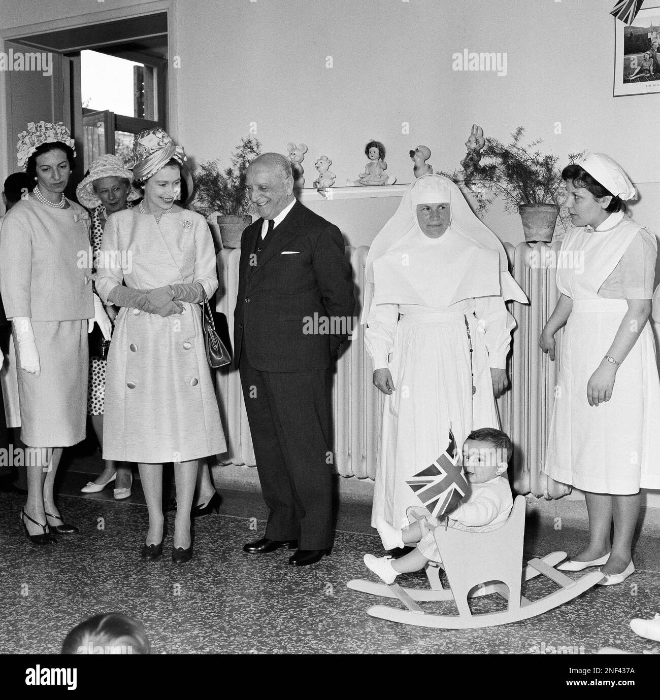 Queen Elizabeth II looks smiling at a small boy who holds a British ...