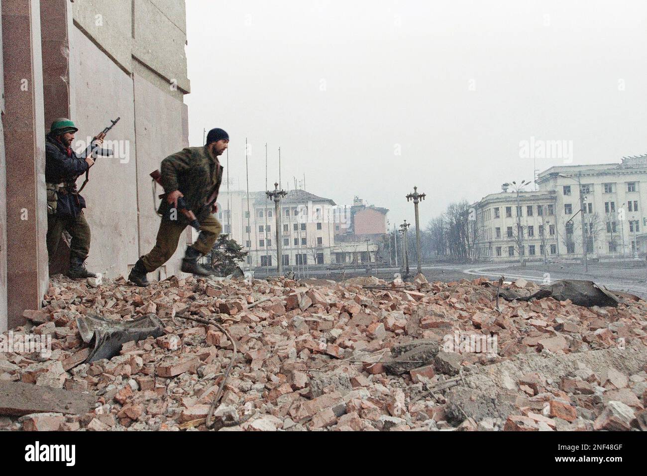 Two Chechen fighters sprint from the presidential palace through rubble ...