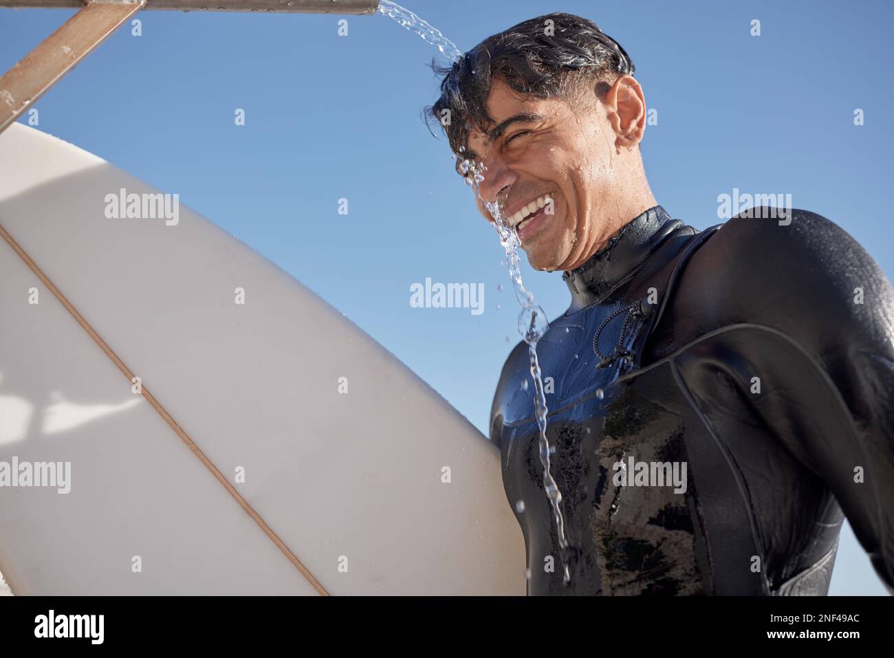 Man, surfing and water shower at beach on face, smile or blue sky in ...