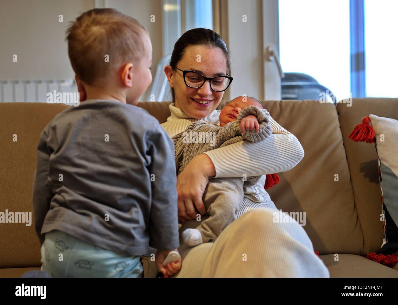 Mother with little toddler and newborn baby sitting on a sofa Stock ...