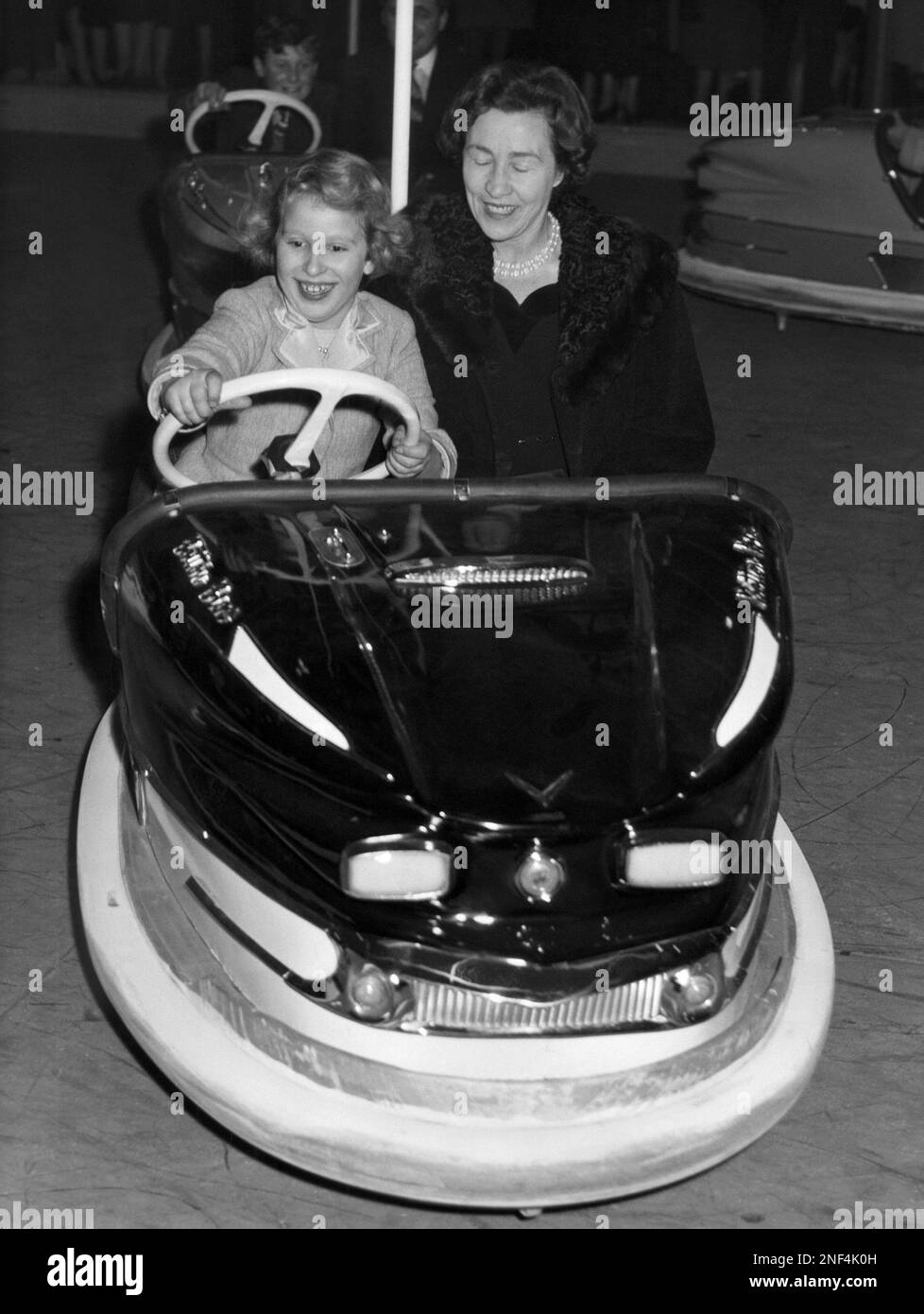 Princess Anne takesa turn at wheel in a "dodgem" car, with Lady Neville ...