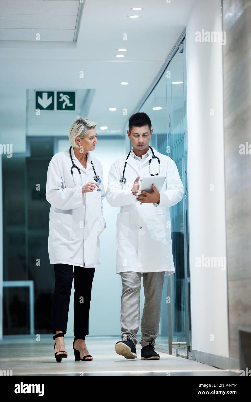 Healthcare, doctors and walking in hospital, tablet and conversation ...