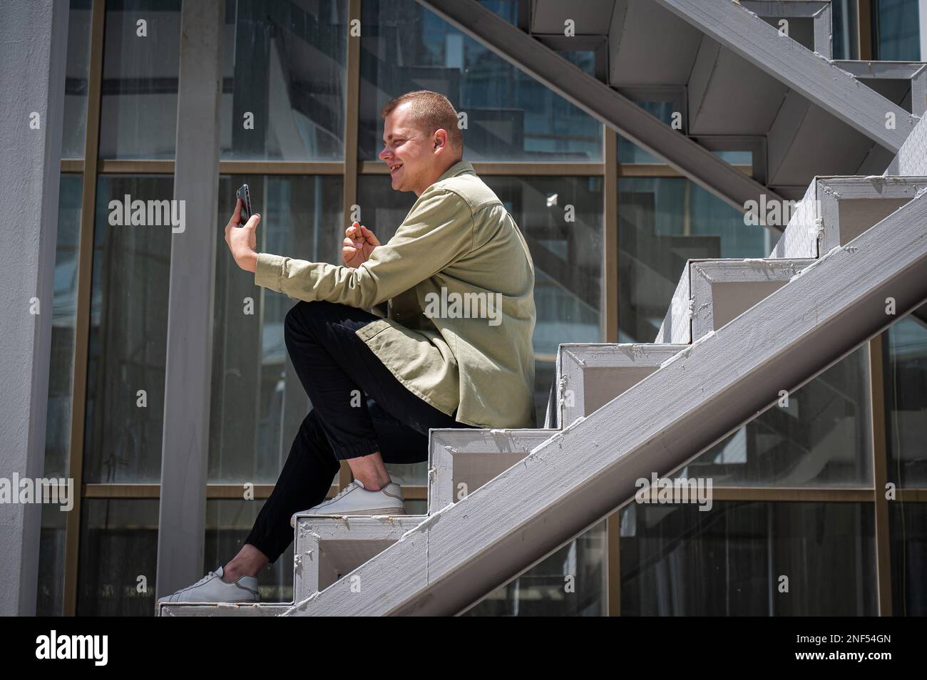 Young man sitting on the stairs and talking sign language via video ...