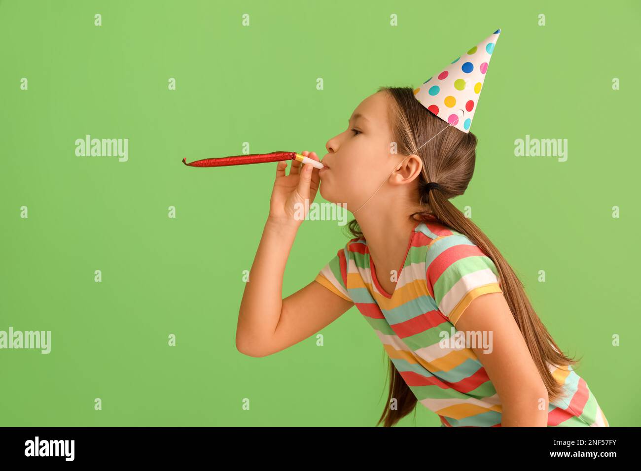 Little girl in party hat with blower on green background. April Fools ...