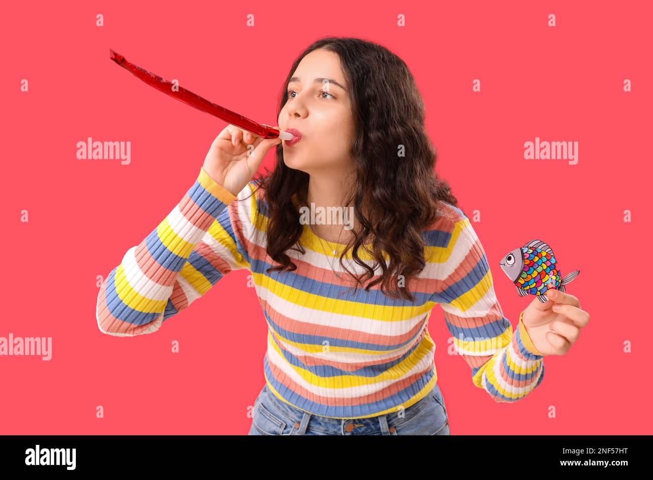 Teenage girl with party blower and paper fish on red background. April ...