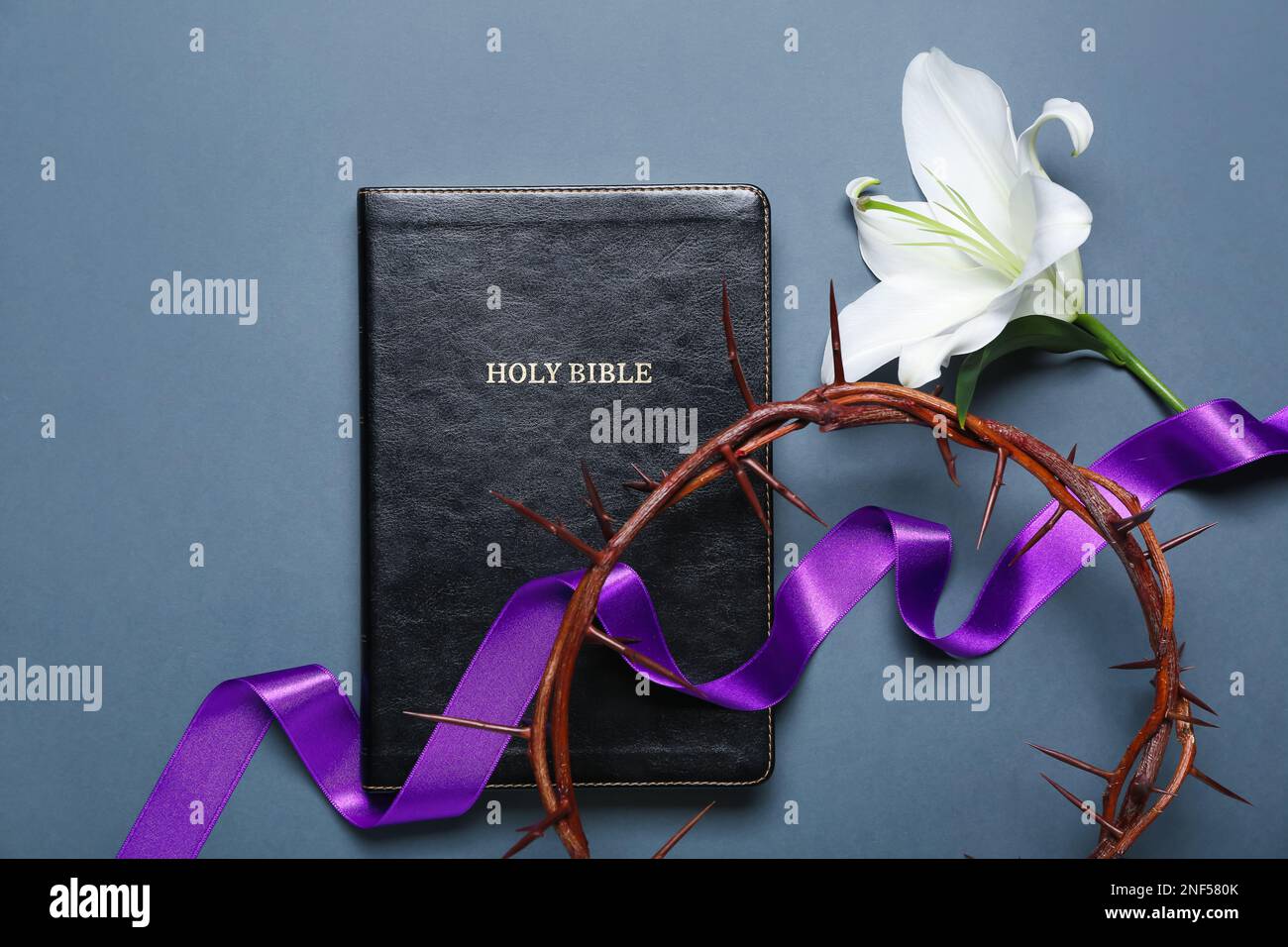 Holy Bible with purple ribbon, crown of thorns and lily flower on blue ...