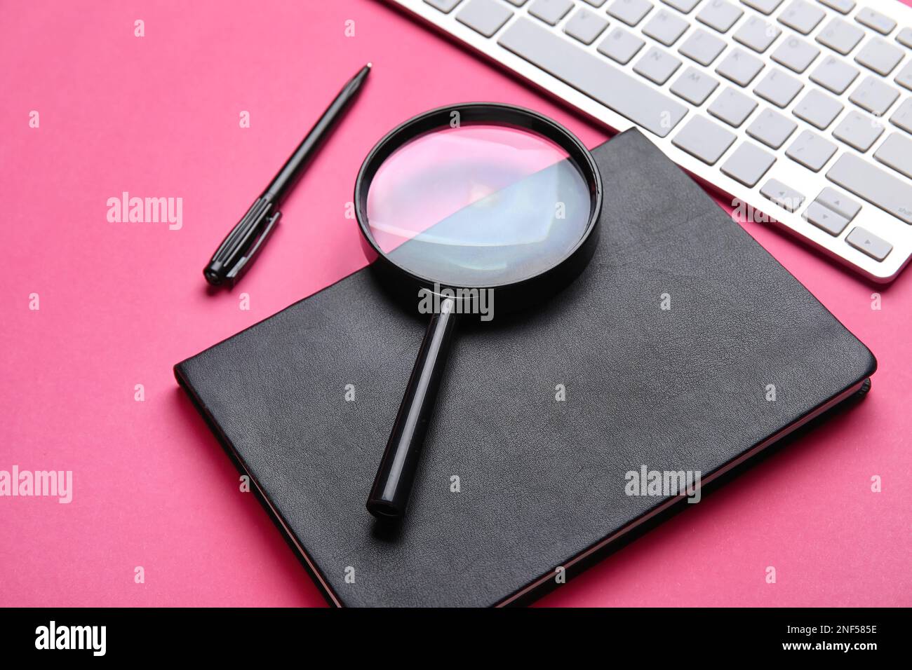 Notebook, pen, magnifier and keyboard on pink background, closeup ...