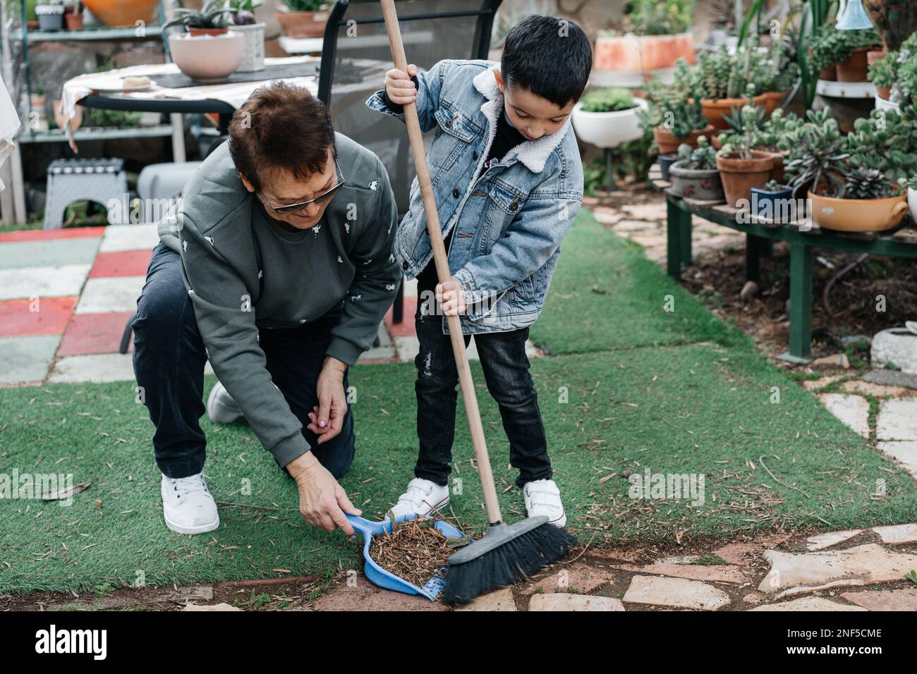 Child helping grandmother and sweeping dry leaves from front yard ...