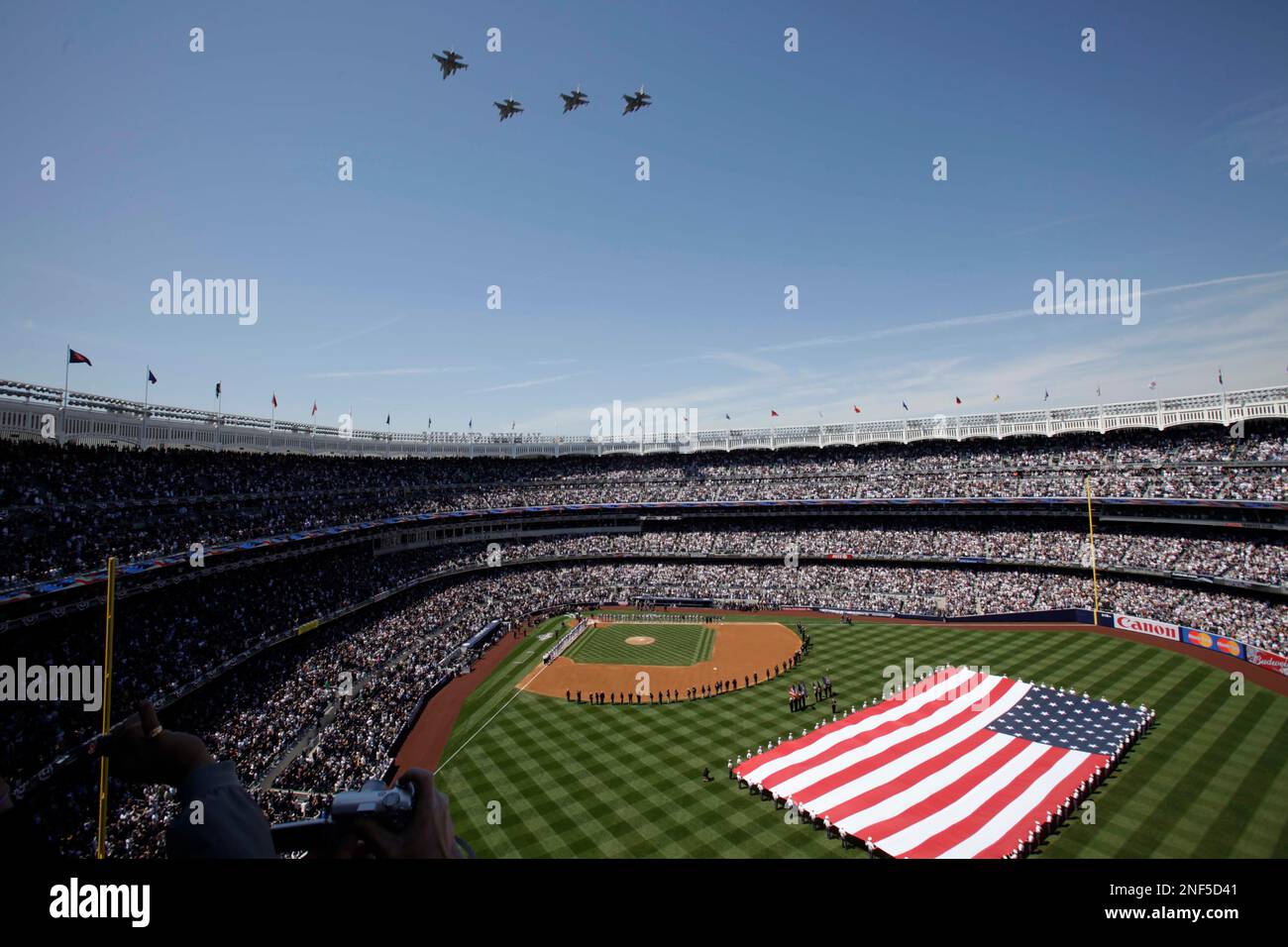 Military jets fly overhead as a large flag is unfurled in center field ...