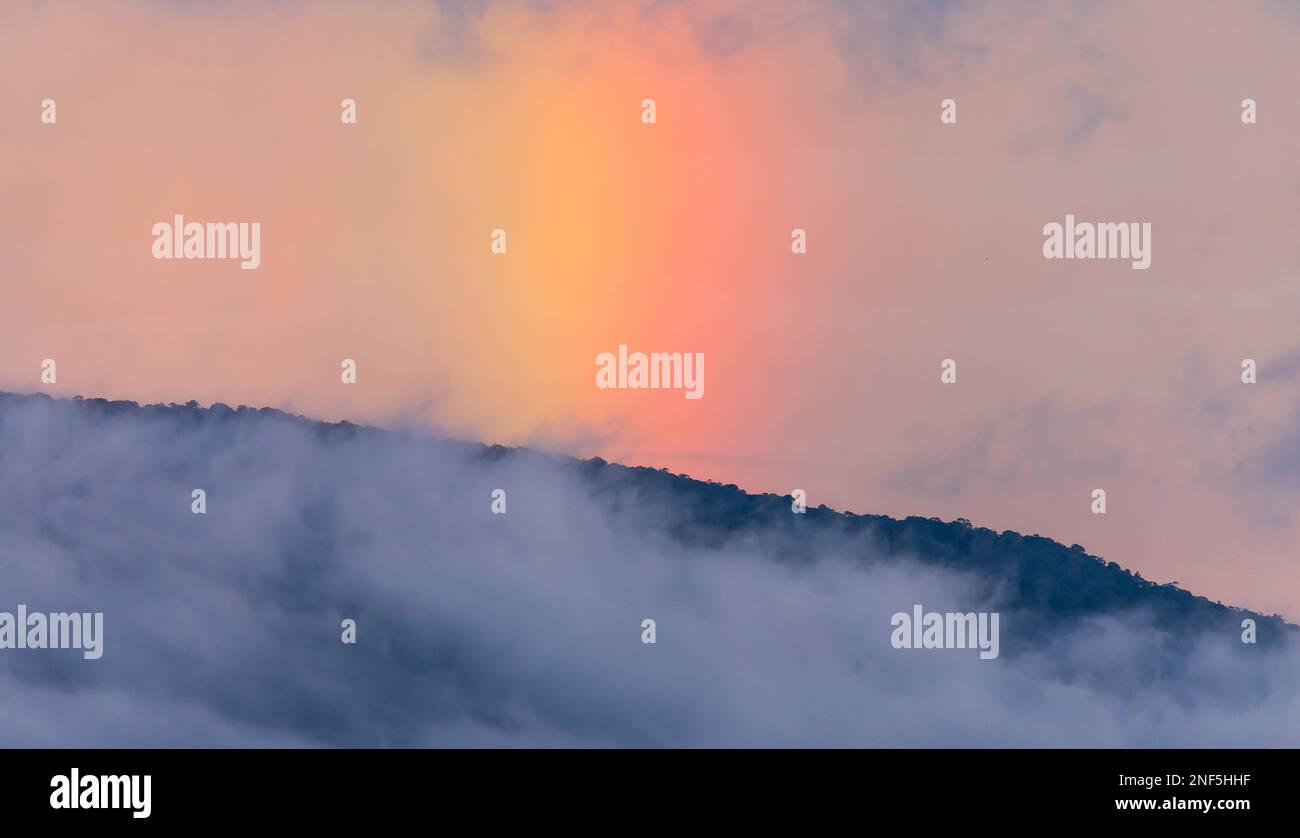 Dramatic sky shining rainbow behind the foggy mountain after raining at ...