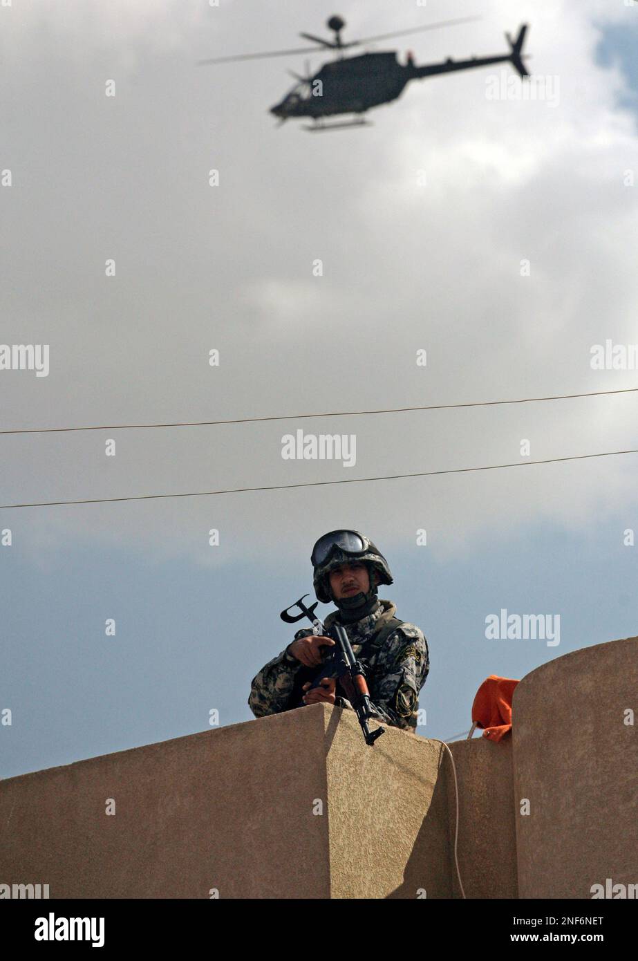 An Iraqi policeman stands guard atop a roof as a U.S. military attack ...