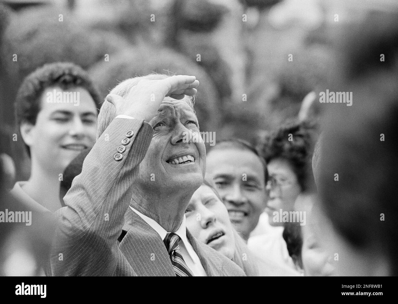 Former U.S. President Jimmy Carter shields his eyes from the bright sun ...