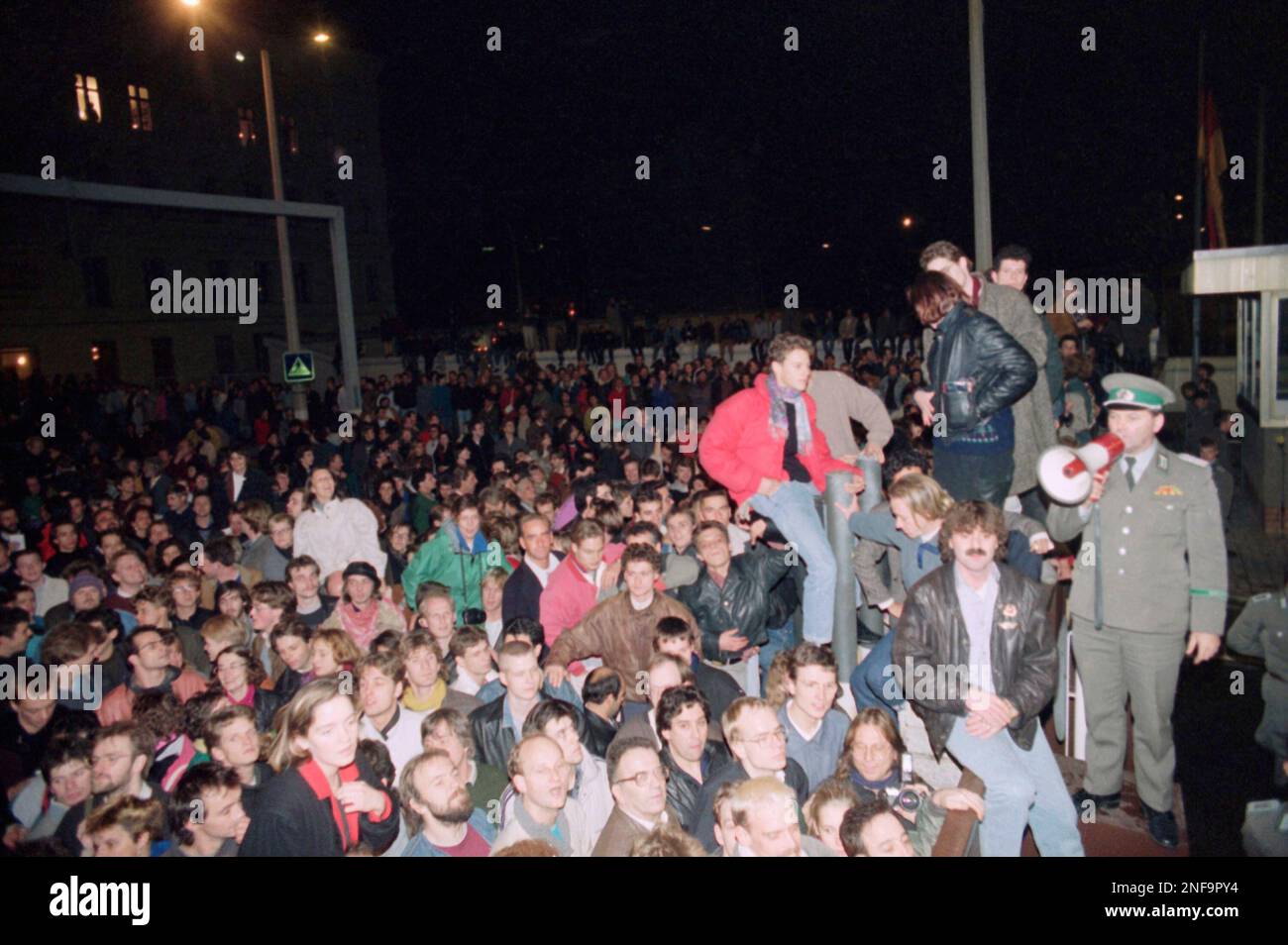 Berliners from East and West crowd the area in front of a border fence ...