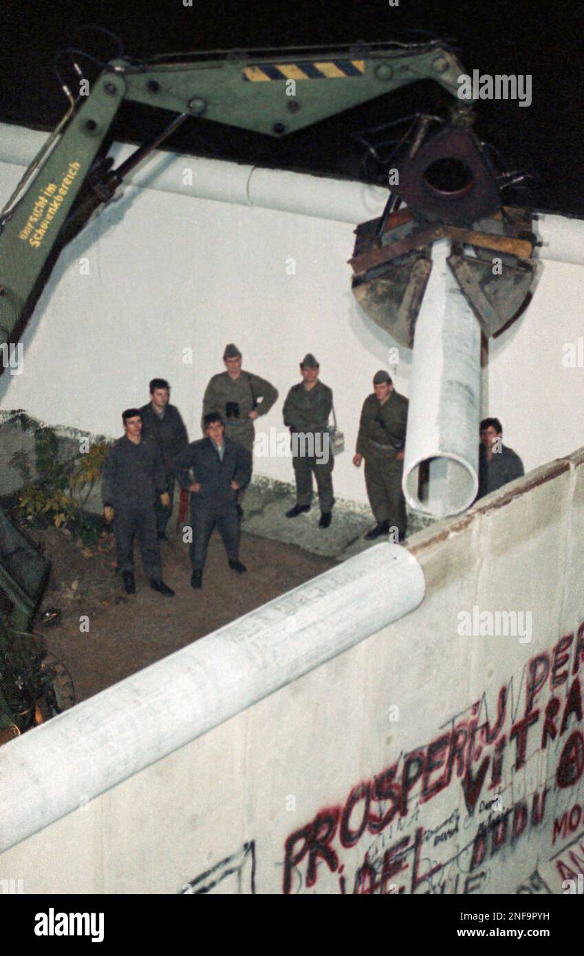 East German border guards watch a bulldozer tear down parts of the ...