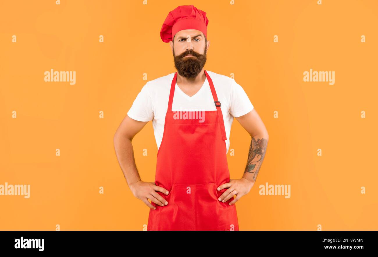 Serious man in red toque and apron with arms akimbo yellow background ...