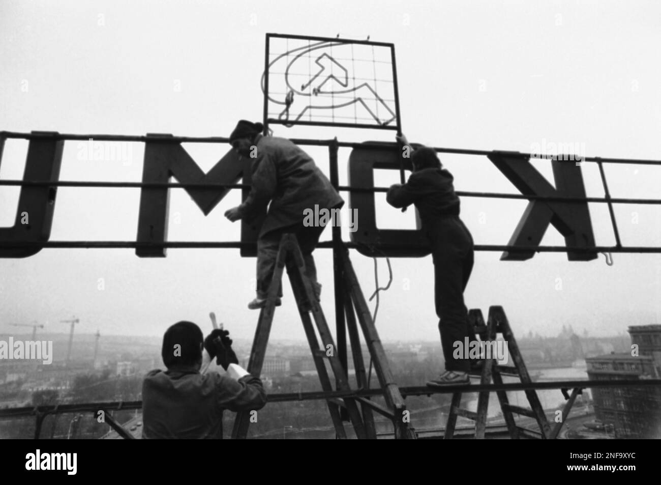 Workers remove a hammer and sickle from a neon sign which reads "Glory ...