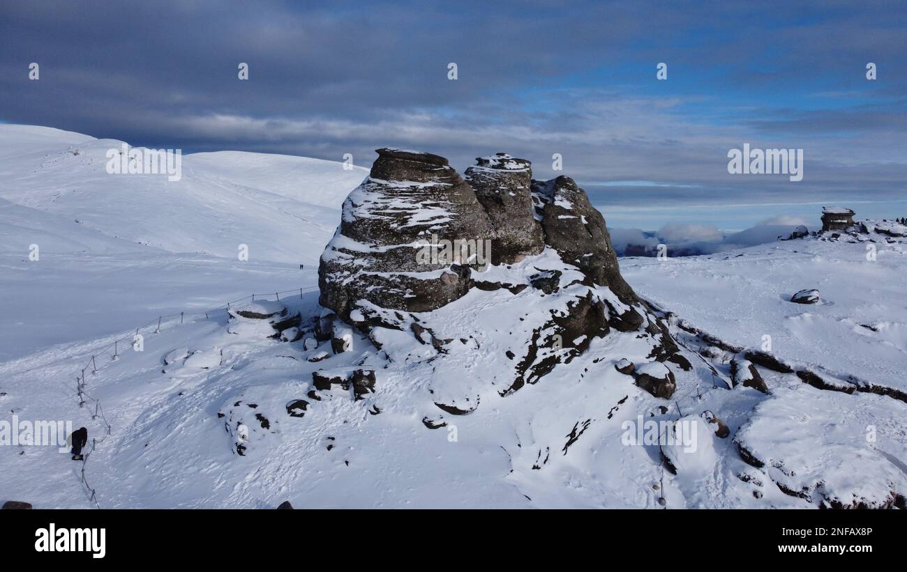 An aerial shot of the sphinx of Bucegi surrounded by mountains in snow ...