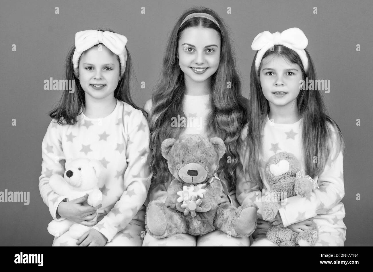 Happy girl children holding teddy bears sitting together in homewear ...