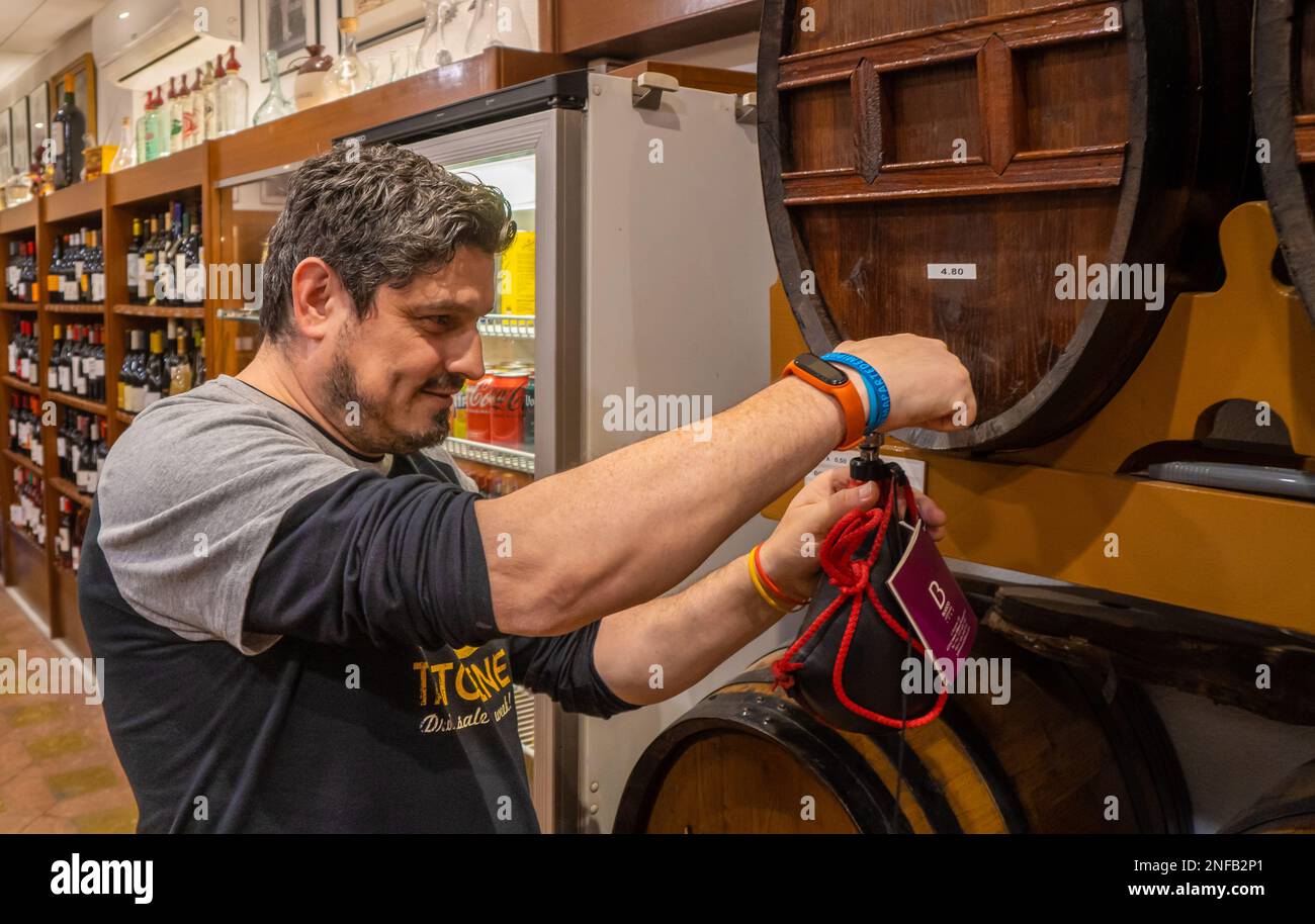 Happy cheerful sommelier filling a leather wineskin from a wooden ...
