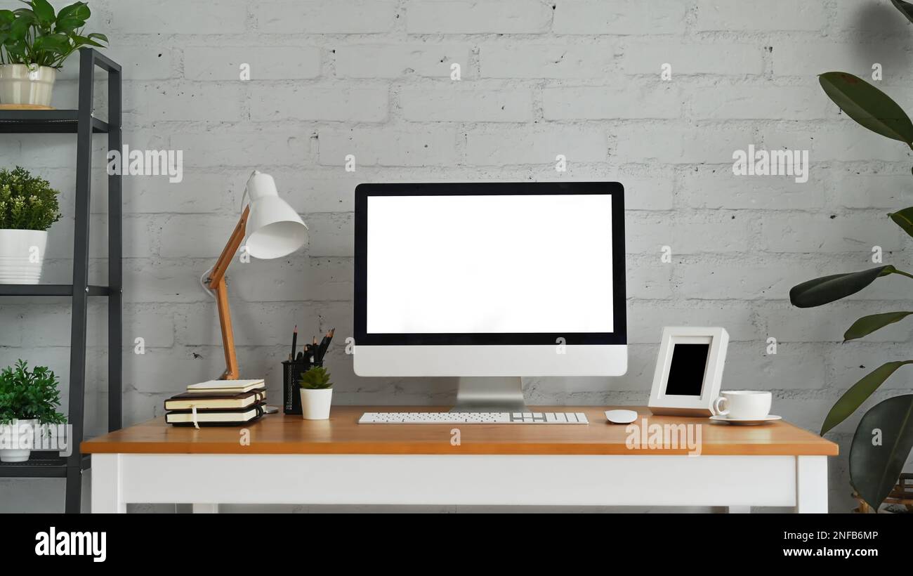 Front view of blank computer screen, lamp and supplies on wooden desk ...