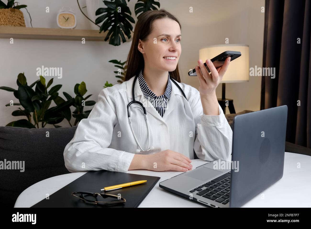 Smiling beautiful young woman doctor recording audio message on ...