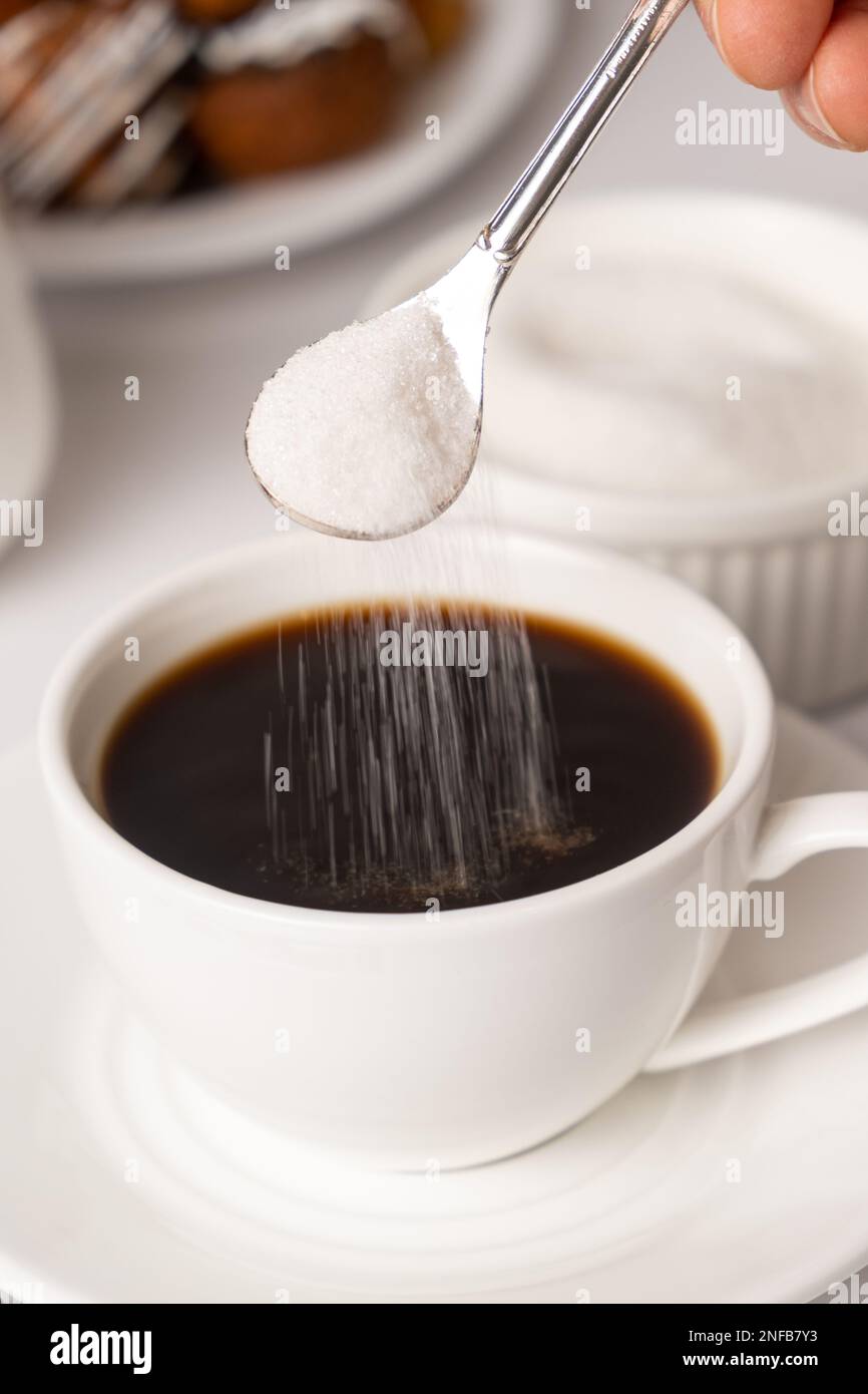 The process of pouring white sugar from a spoon into a white cup of ...