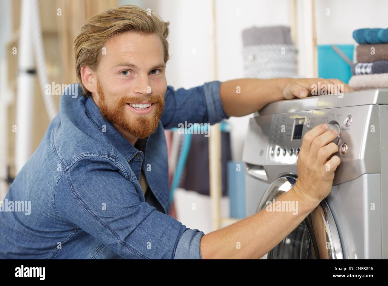 young man loading clothes into washing machine in kitchen Stock Photo ...