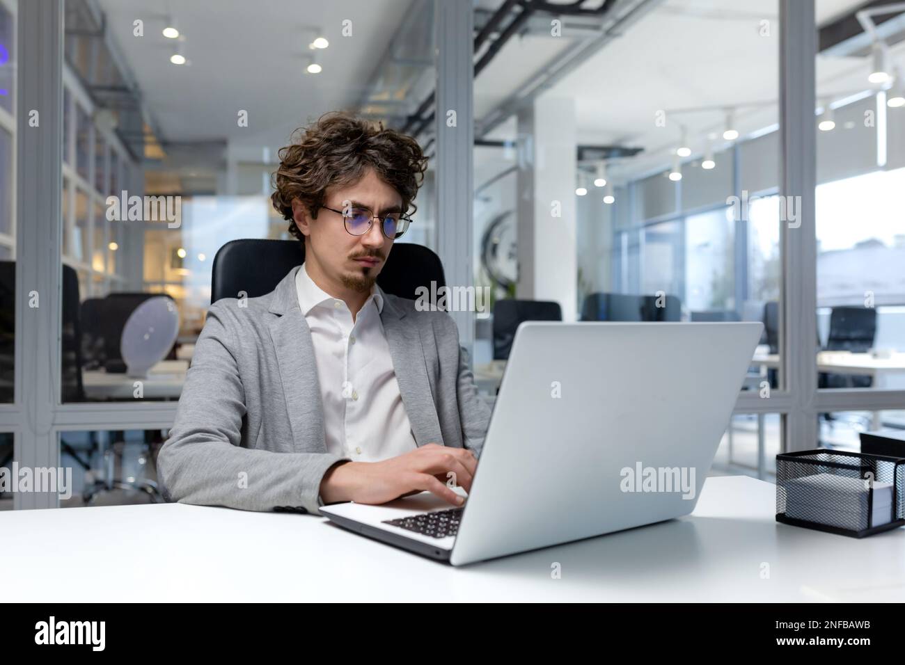 Serious and focused businessman inside modern office working on laptop, bearded man typing on ...