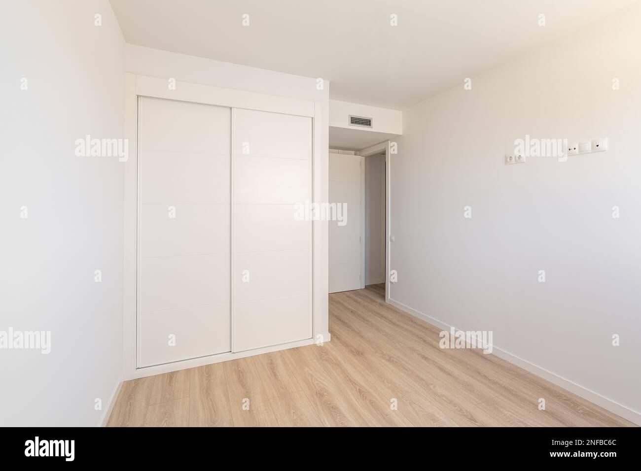 White empty sunny room with built-in wardrobe ventilation and two doors ...