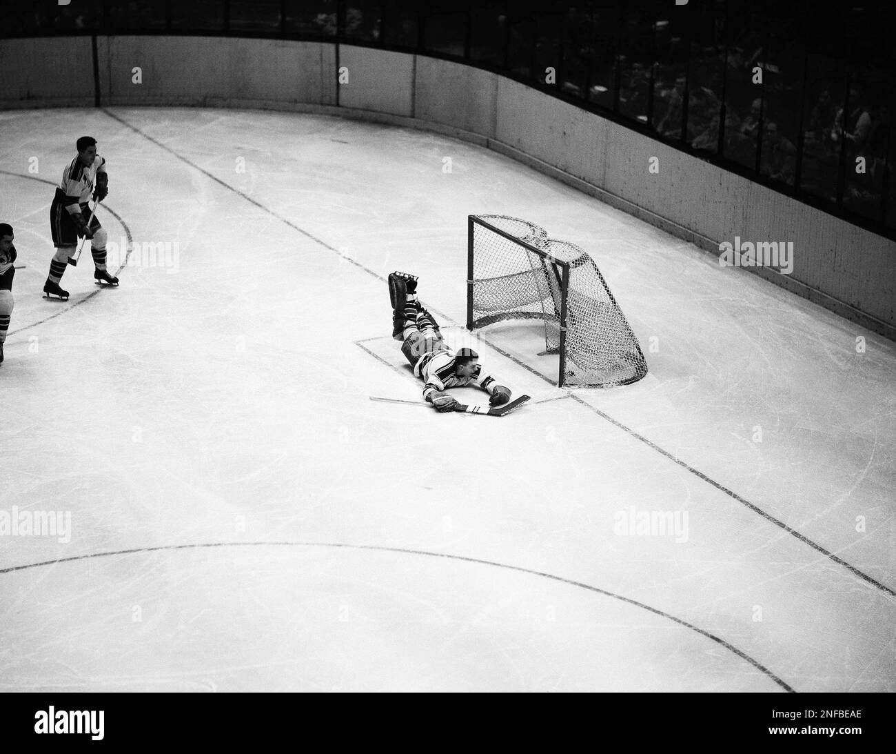 New York Rangers goalie Lorne Worsley lies flat on the ice as he peers ...