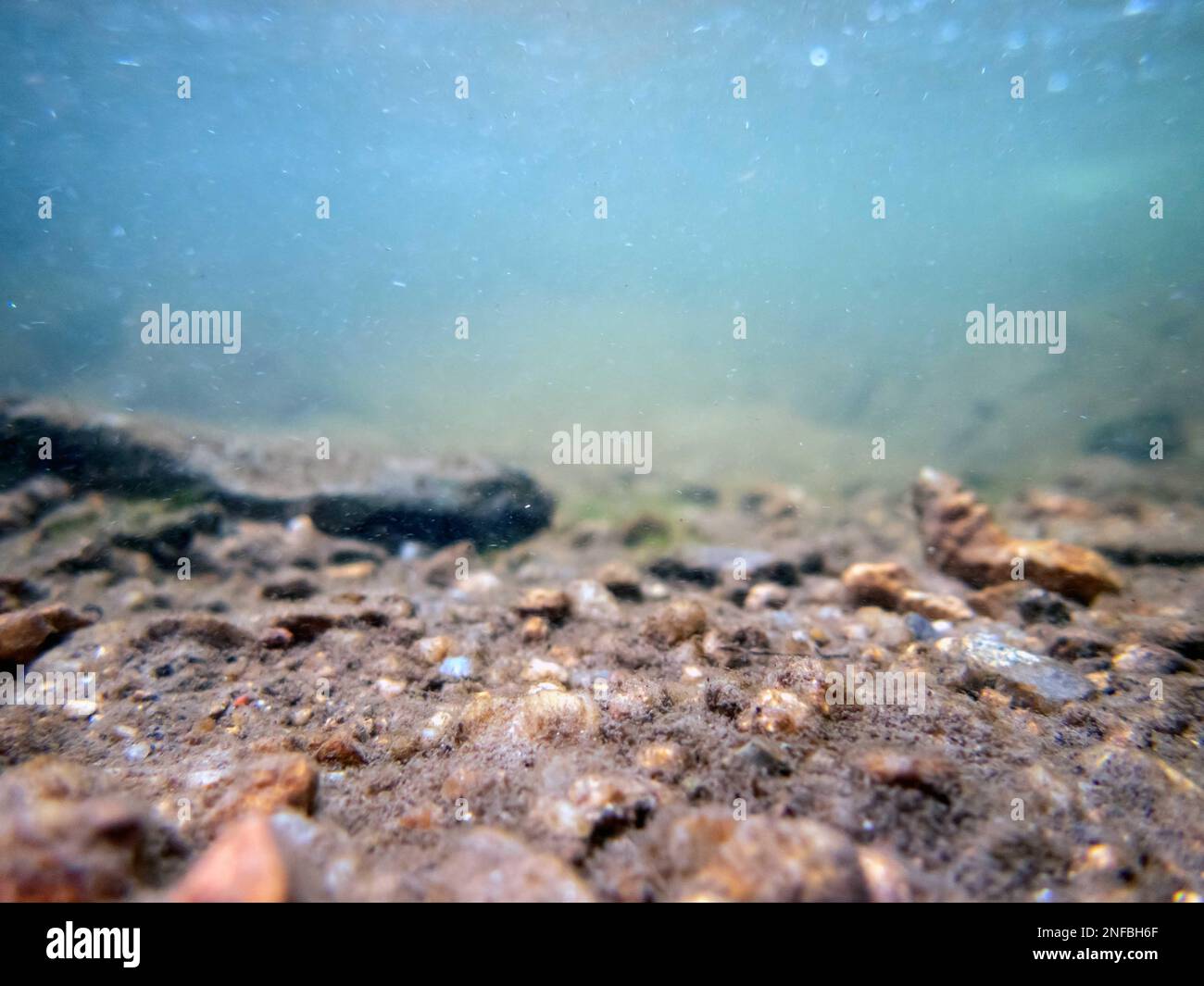 Blue-green flowing water ripples and bubbles over colorful textured ...