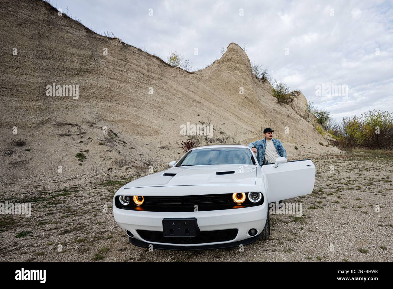 Handsome man in jeans jacket and cap is standing near his white muscle ...