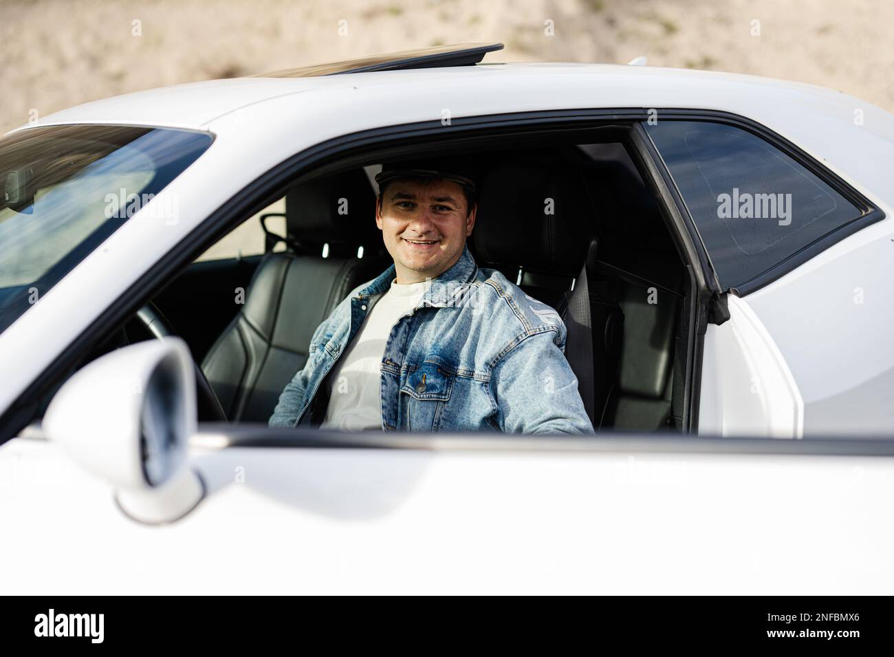 Handsome man in jeans jacket and cap sit at his white muscle car Stock ...
