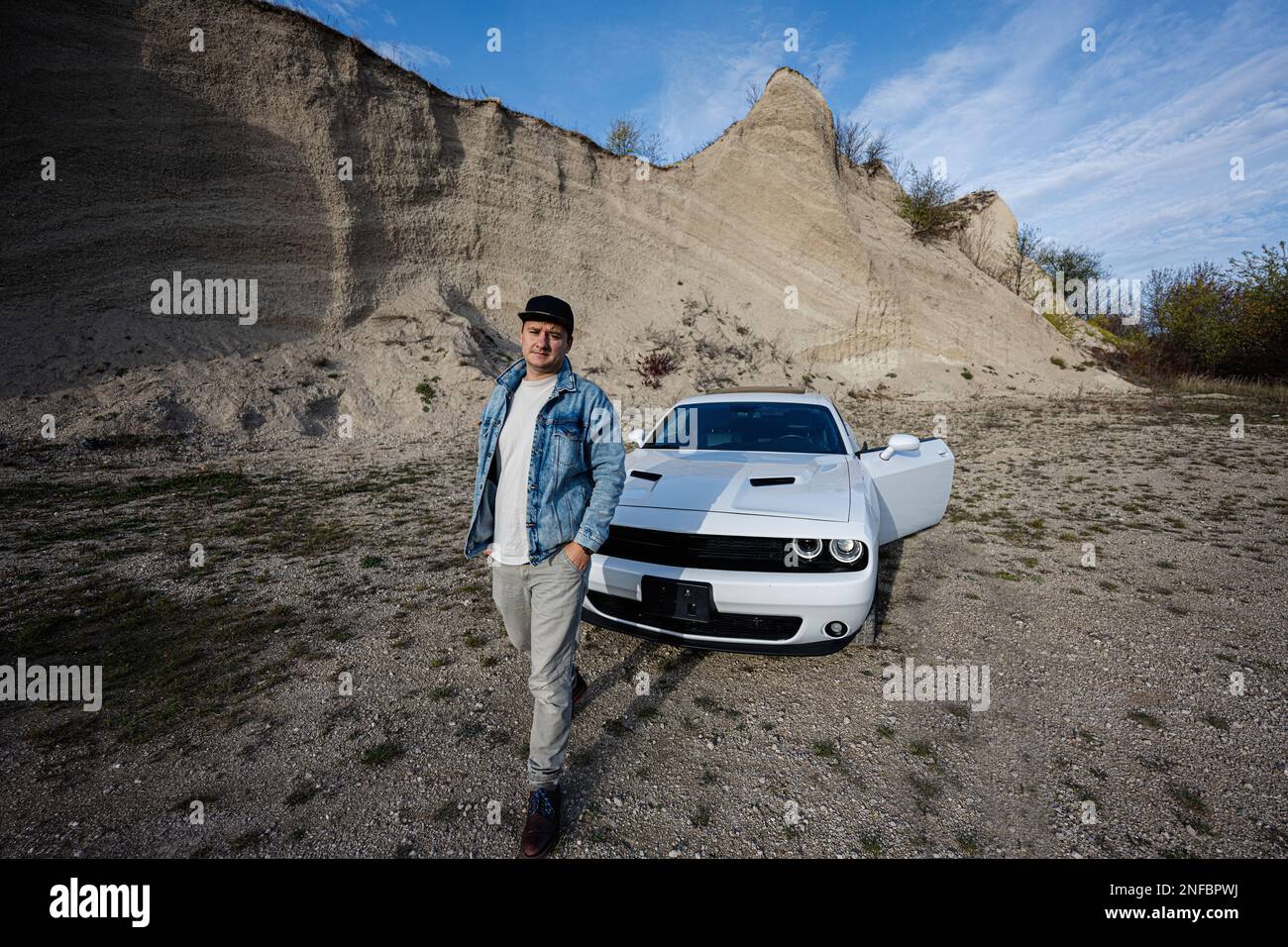 Handsome man in jeans jacket and cap is standing near his white muscle ...
