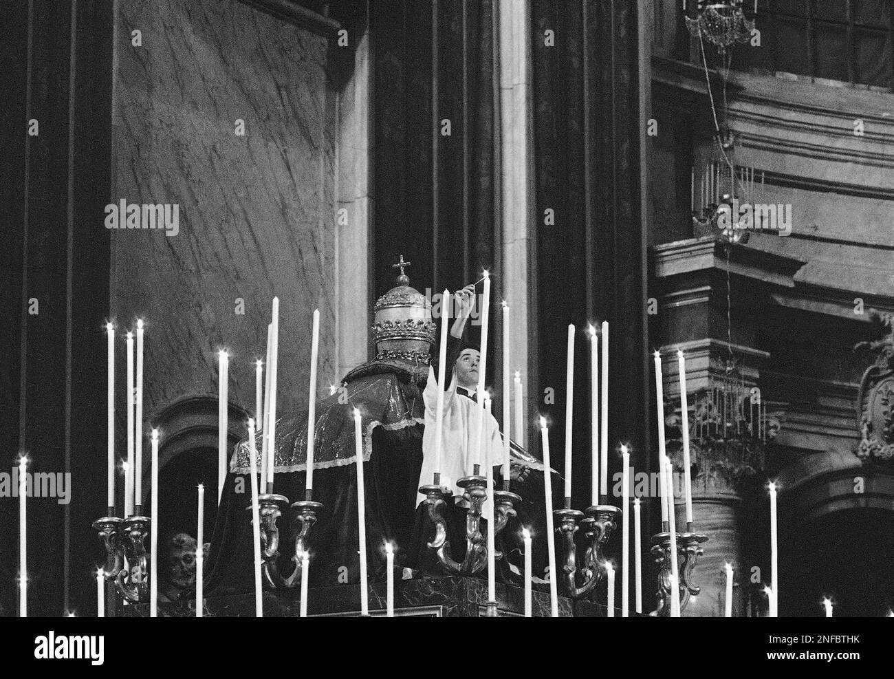 An altar boy lights candles at tall catafalque atop of which is ...
